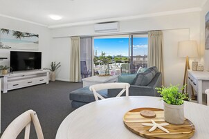 Uma sala de estar moderna com televisão de tela plana, mesa de jantar com cadeiras, sofá e varanda com vista para a cidade.