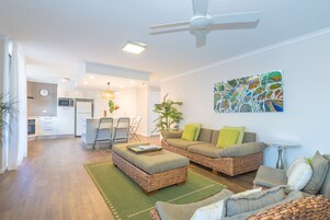 Uma sala de estar moderna com móveis de vime, uma área de jantar e uma cozinha ao fundo.