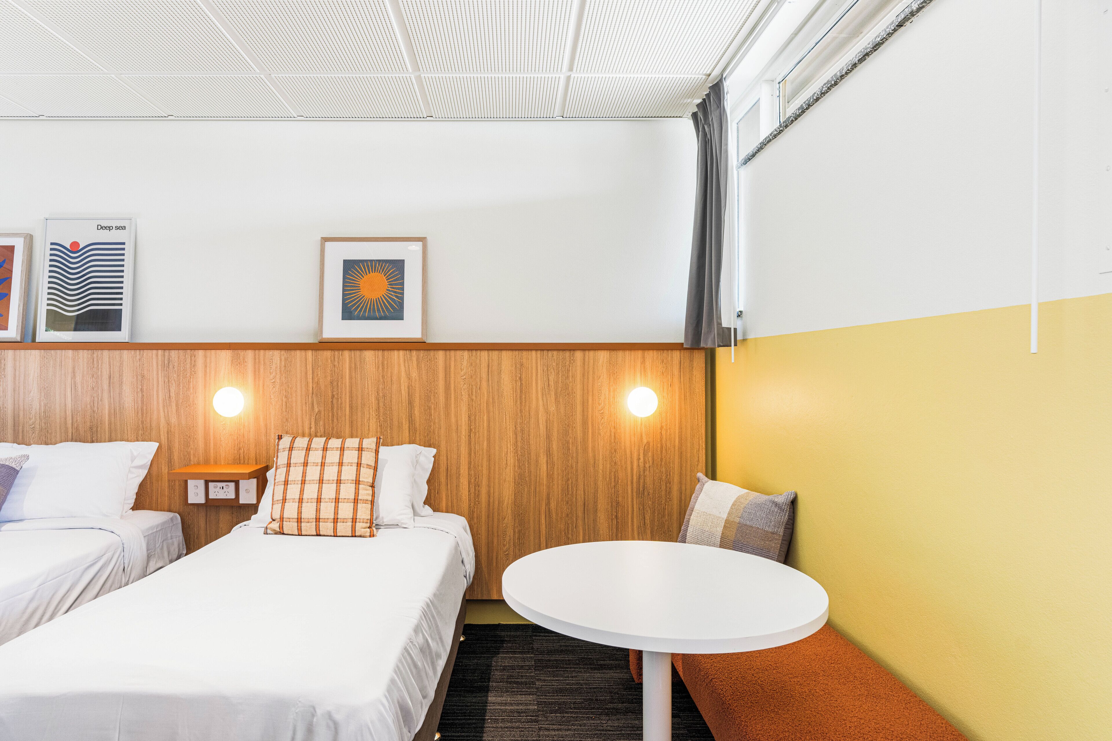 Quarto de hotel com duas camas, uma mesa redonda e obras de arte penduradas na parede.