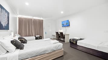 Quarto de hotel com uma cama grande, uma escrivaninha, uma cadeira e uma televisão na parede.
