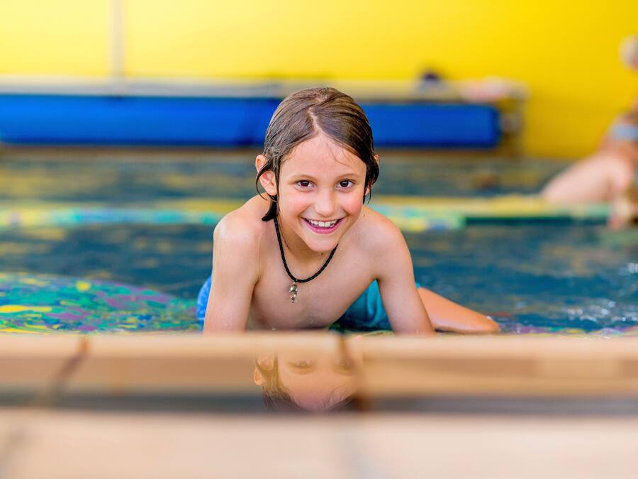 Criança em uma piscina com fundo azul e amarelo.