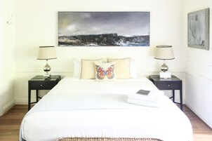 Quarto de hotel bem organizado, com uma cama grande, duas mesas de cabeceira com abajures, uma pintura de paisagem urbana acima da cama e uma obra de arte emoldurada na parede.