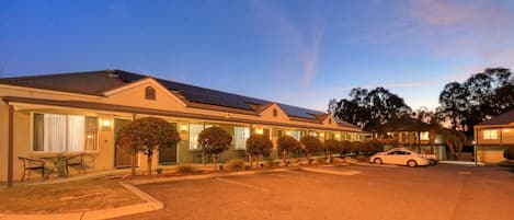 Fileira de edifícios de motel com painéis solares, área de estacionamento coberta e um carro estacionado na frente.