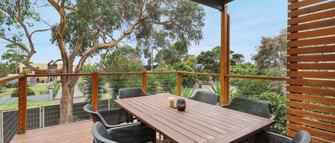Um deck de madeira com uma mesa e cadeiras, com vista para um jardim e área residencial.