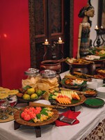 Uma mesa com diversos pratos e alimentos, incluindo frutas e petiscos, dispostos sobre uma toalha.