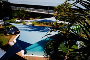 Uma piscina com espreguiçadeiras, uma palmeira e um edifício ao fundo.