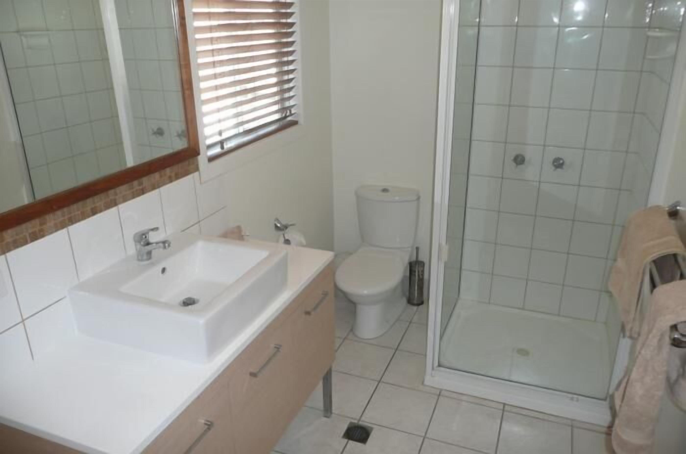 Casa de banho com lavatório branco, sanita e cabine de duche com vidro.