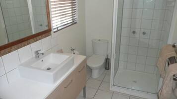 Casa de banho com lavatório branco, sanita e cabine de duche com vidro.
