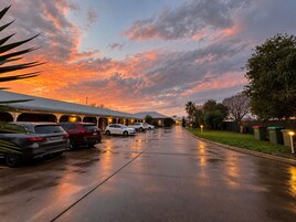 Hotel com estacionamento coberto, fileira de carros estacionados e edifício com telhado plano.