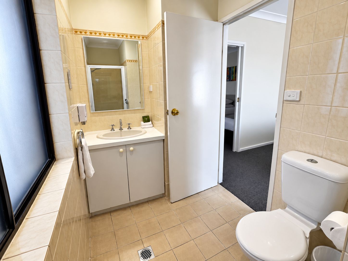 Casa de banho com lavatório, espelho, sanita e porta para outro quarto.
