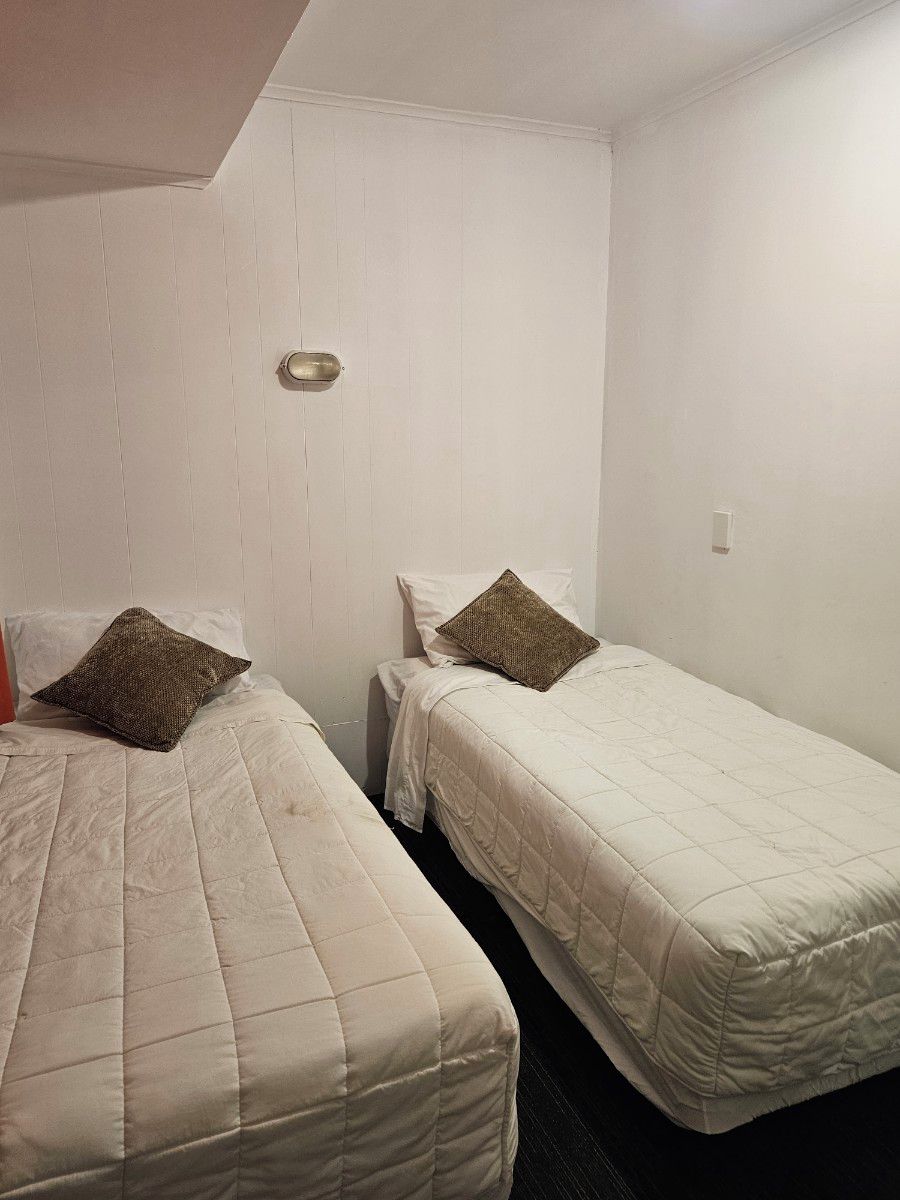 Quarto pequeno e limpo com duas camas individuais, cada uma com uma almofada e mesa de cabeceira.