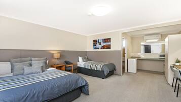 Quarto de hotel com duas camas, uma mesa, frigorífico e cozinha compacta.