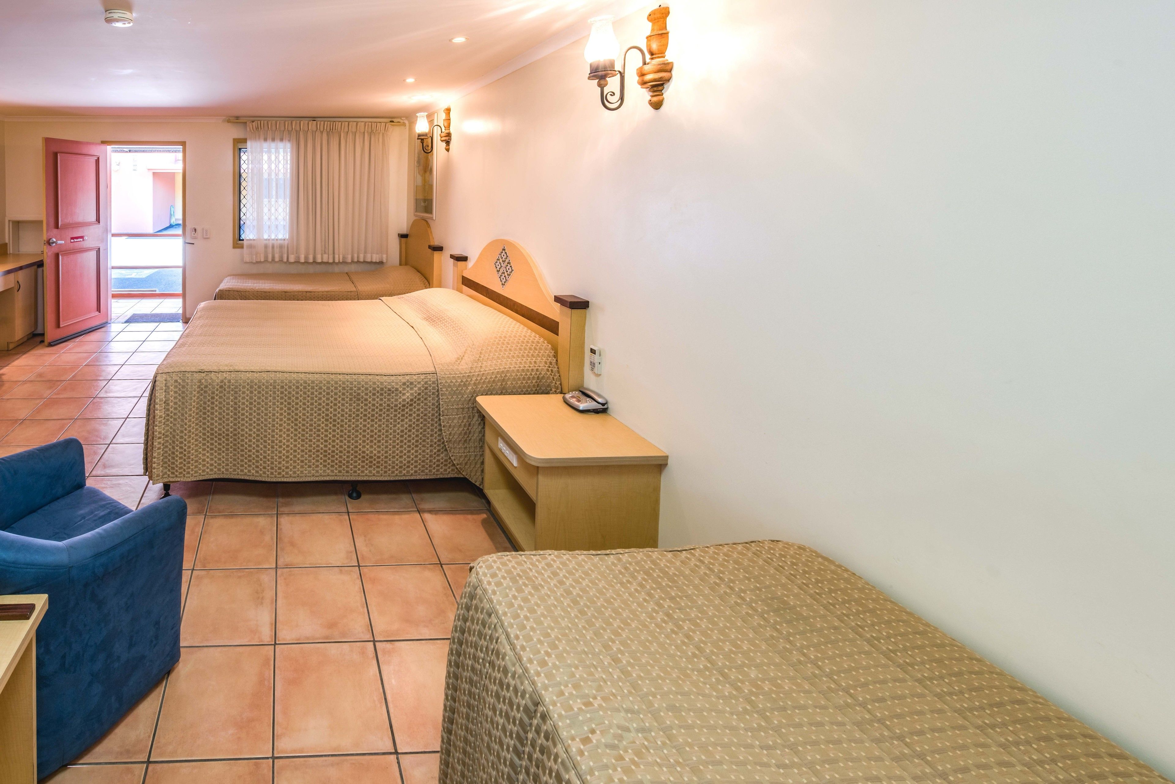 Quarto de hotel com duas camas, uma escrivaninha, uma cadeira e um banheiro visível por uma porta aberta.