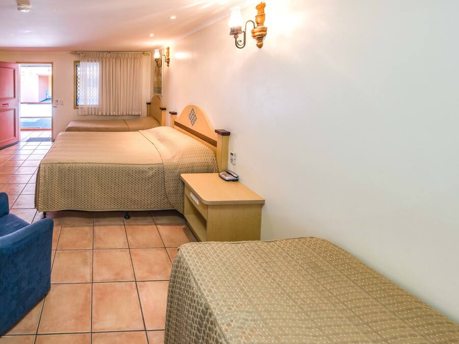 Quarto de hotel com duas camas, uma escrivaninha, uma cadeira e um banheiro visível por uma porta aberta.