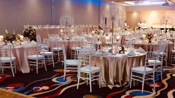 Uma sala de banquetes com mesas redondas, cadeiras brancas e aranjos florais.