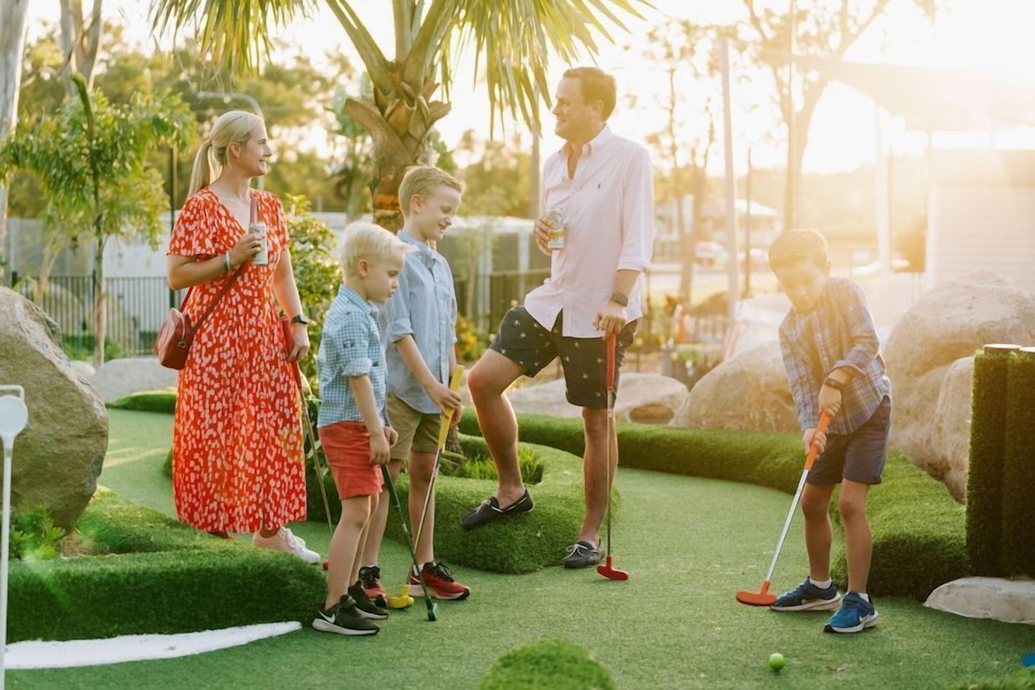 Uma família jogando golfe em um campo bem cuidado, com gramado impecável e pedras grandes.