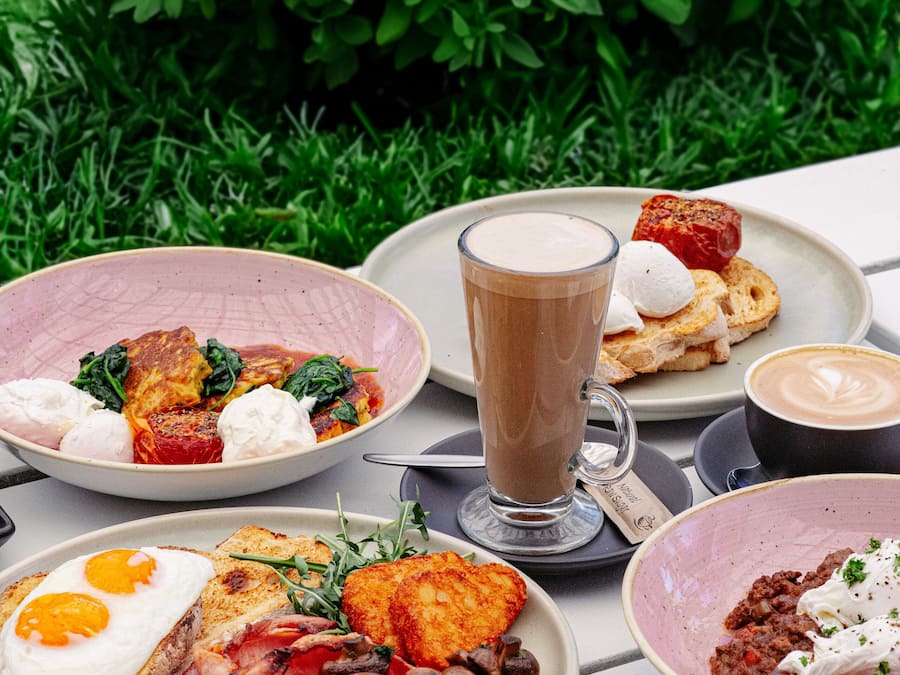 Uma mesa posta com diversos pratos de café da manhã, incluindo ovos, torradas e café.
