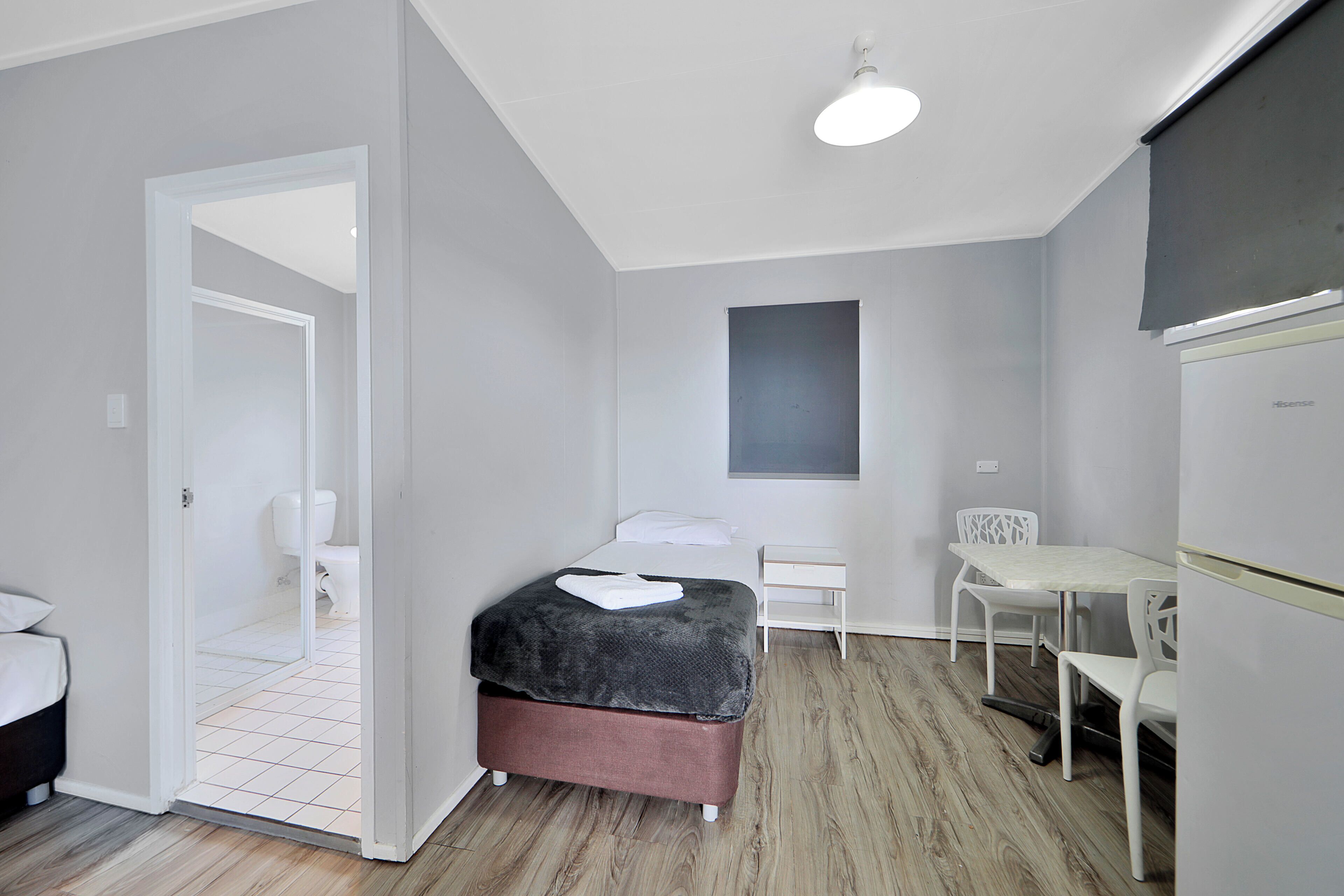 Quarto moderno com cama, mesa de cabeceira e escrivaninha com cadeiras.