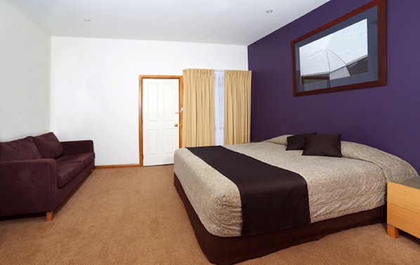 Um quarto com uma cama, um sofá, uma porta e uma janela com cortinas.