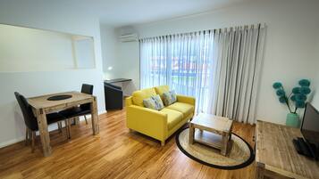 Uma sala de estar mobiliada com uma mesa de jantar de madeira, sofá amarelo e uma pequena mesa de centro.