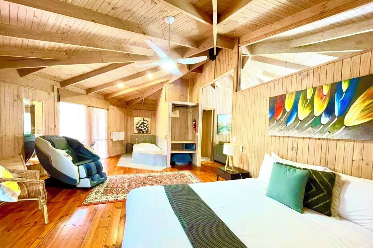 Quarto espaçoso com uma cama grande, poltrona de massagem, banheira e um quadro na parede.
