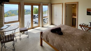 Quarto com cama, escrivaninha e cadeira. Há cortinas e vista para o exterior.