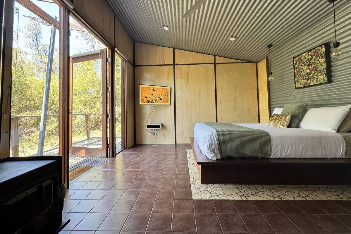 Um quarto com uma cama, um ventilador de teto, um ar condicionado fixado na parede e uma janela grande.