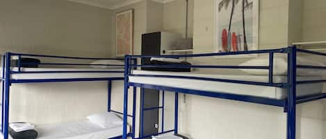 Beliches em um quarto com paredes de tijolos brancos, um quadro e uma escrivaninha com um computador.