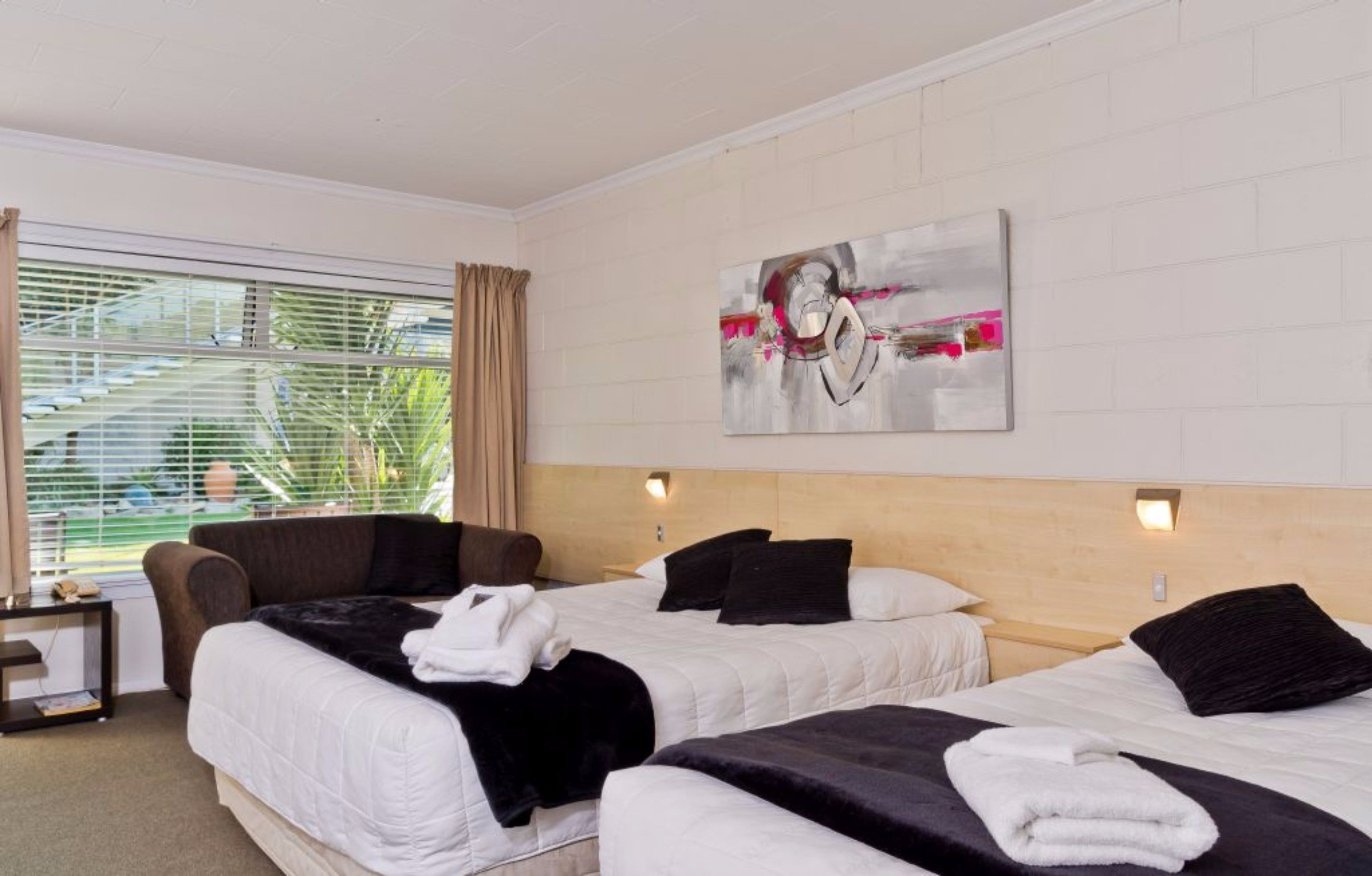 Quarto de hotel com duas camas, um quadro abstrato grande na parede e uma janela com persianas.