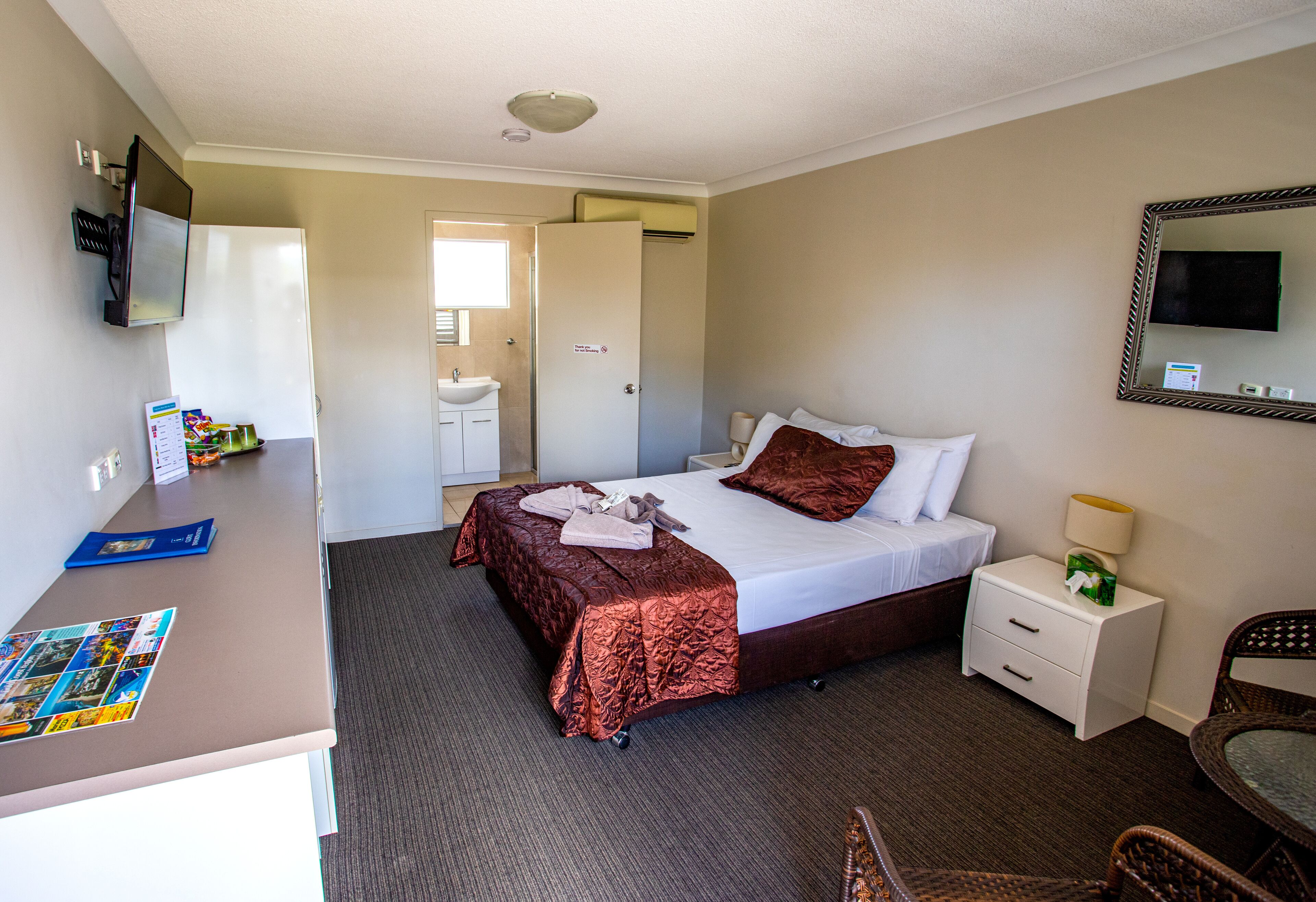 Quarto de hotel com uma cama, uma escrivaninha com computador, uma cadeira e uma pequena mesa.