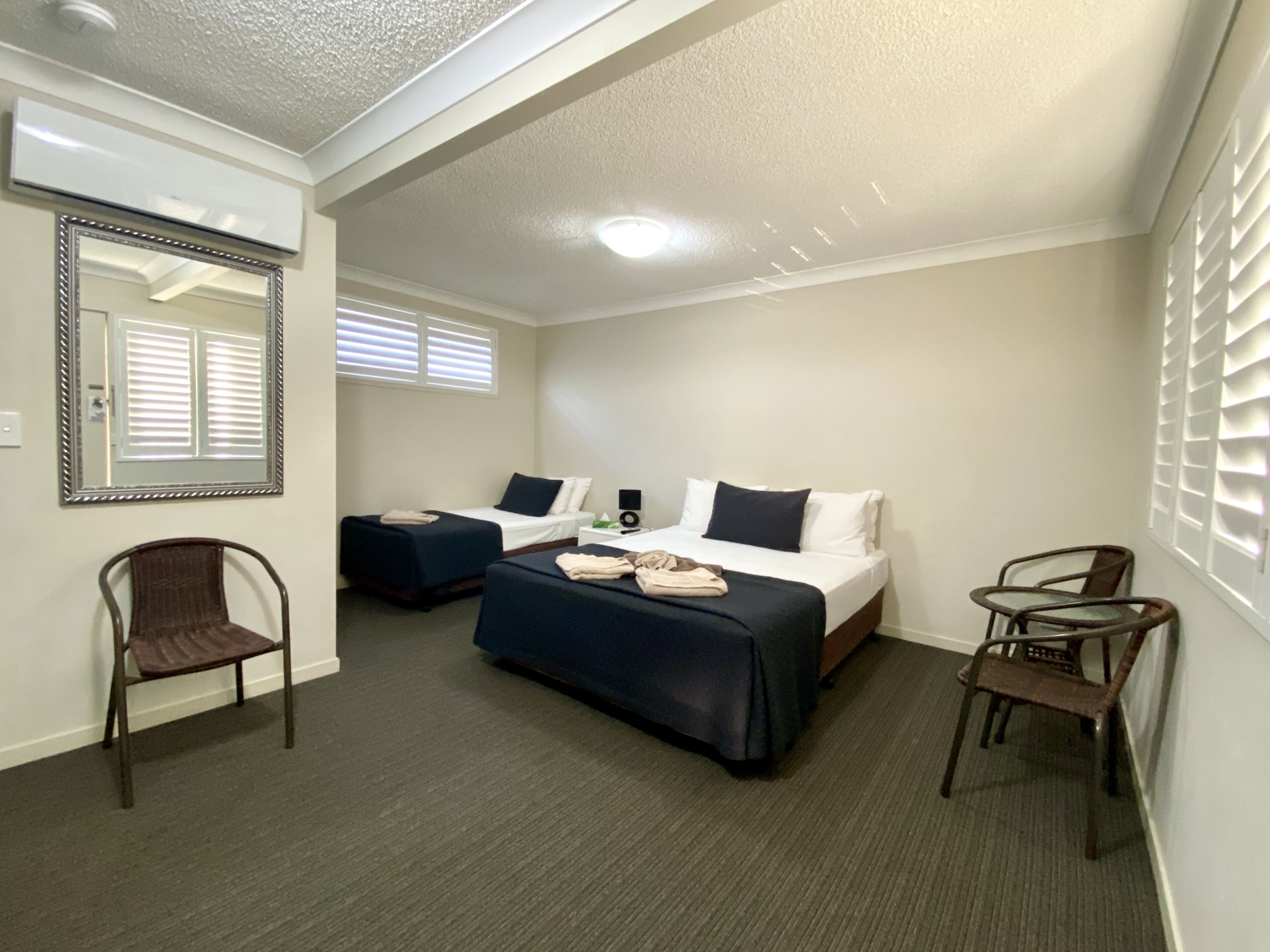 Quarto de hotel com duas camas, um espelho grande, uma cadeira e uma mesa pequena.