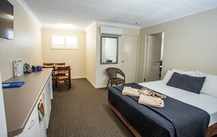 Quarto de hotel com cama, escrivaninha, cadeira, mesa pequena e janela.
