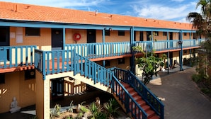Um motel de dois andares com telhado de telhas vermelhas, grades azuis e uma escadaria central.