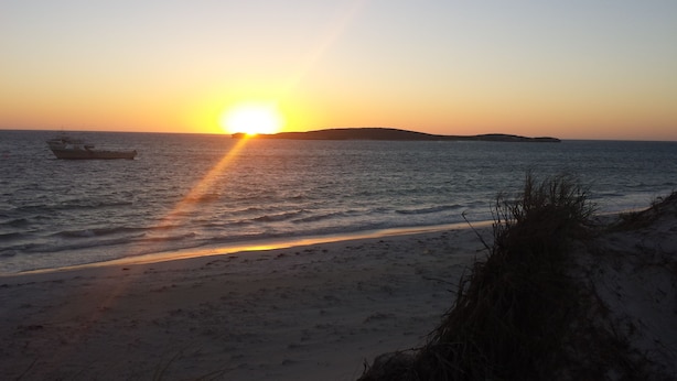 Uma praia com um barco na água e um pôr do sol ao fundo.