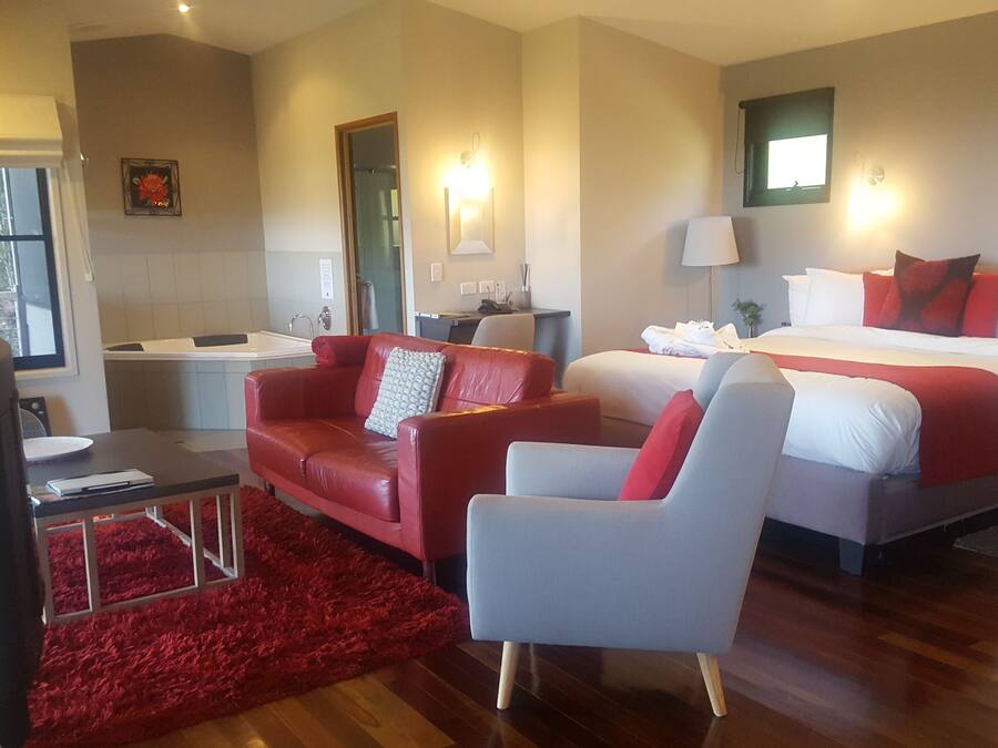 Quarto de hotel moderno com esquema de cores vermelho e branco, apresentando um sofá, poltronas, uma cama, uma escrivaninha e um banheiro com banheira.