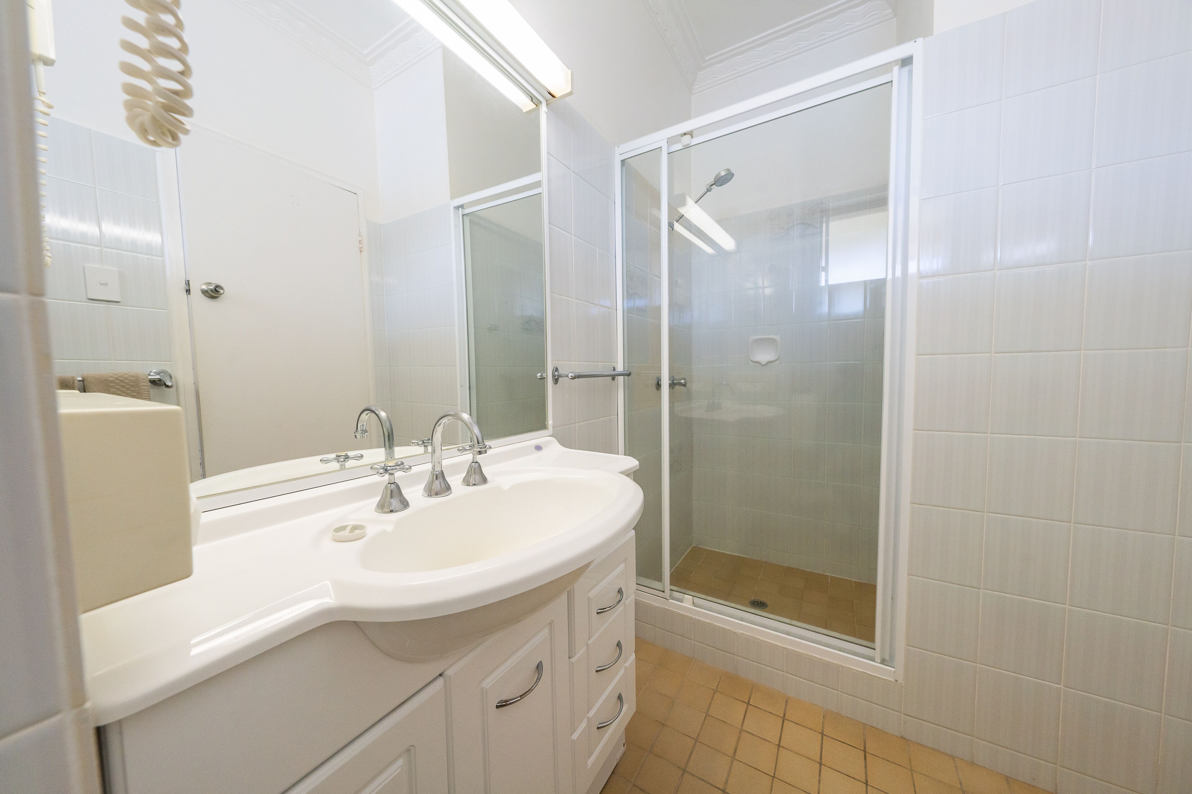 Casa de banho com lavatório branco, espelho e cabine de duche em vidro.