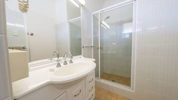 Casa de banho com lavatório branco, espelho e cabine de duche em vidro.