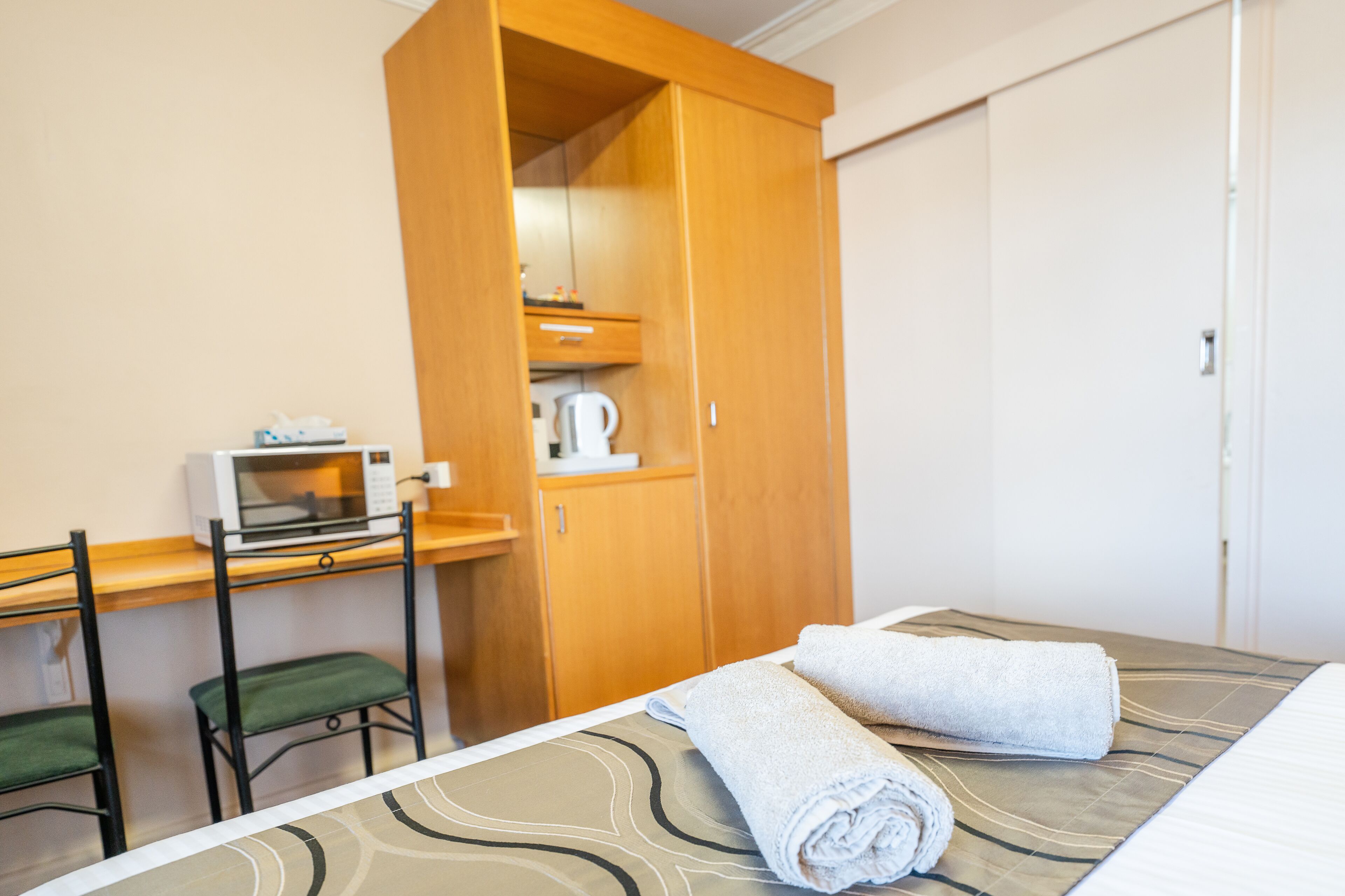 Quarto de hotel com cama, micro-ondas, chaleira e roupeiro de madeira.