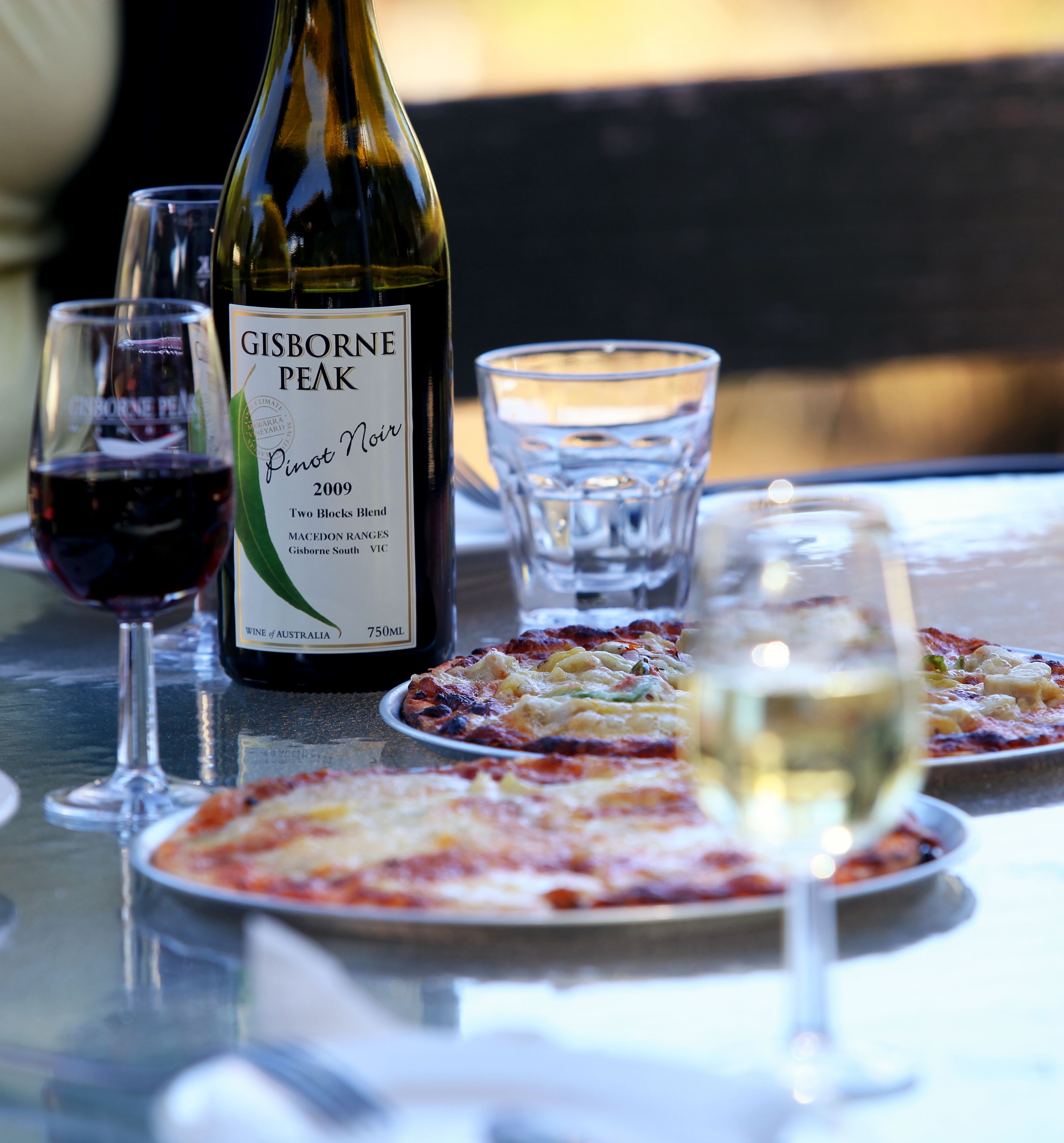 Uma mesa com duas pizzas, uma garrafa de vinho e copos.