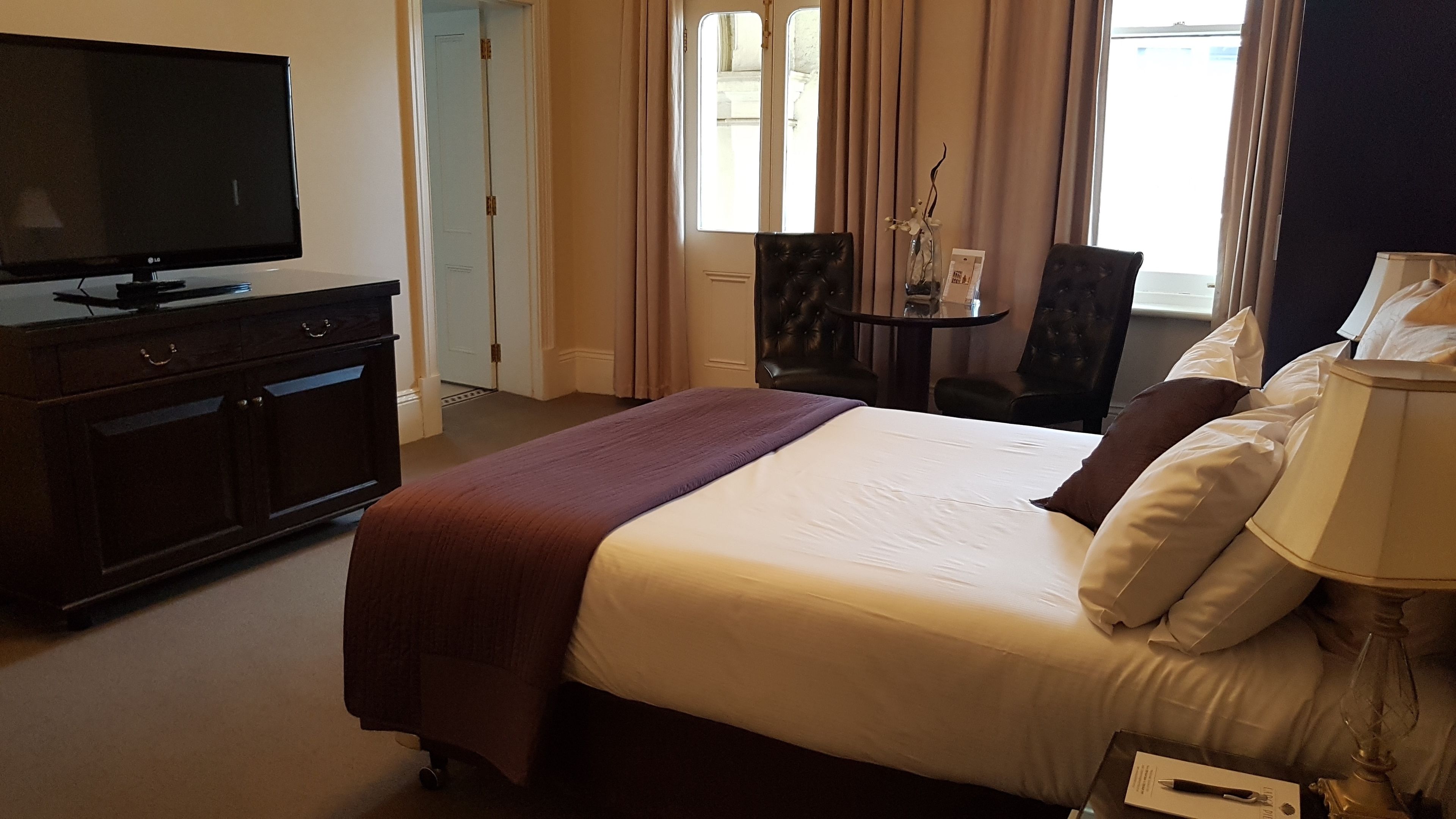 Quarto de hotel com cama, televisão, escrivaninha e cadeira.