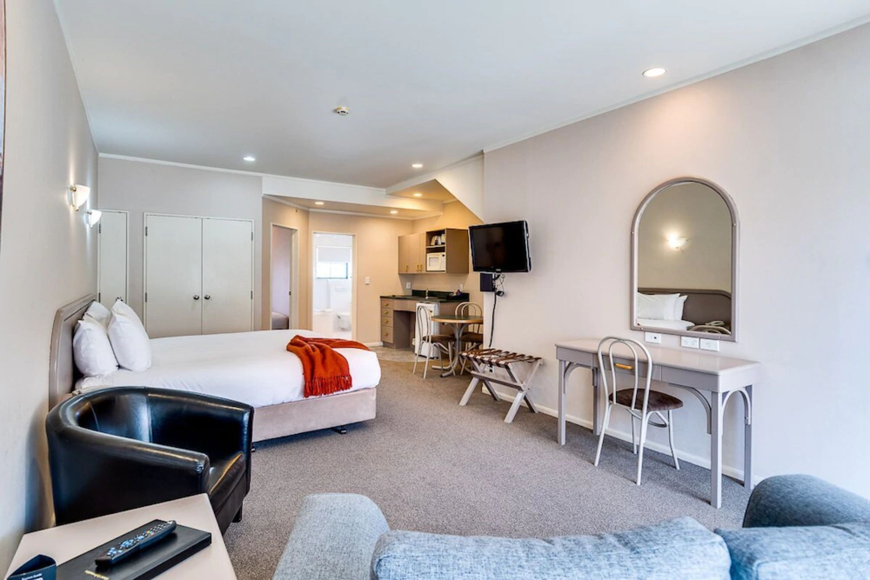 Quarto de hotel com uma cama, escrivaninha, cadeira, televisão e espelho.