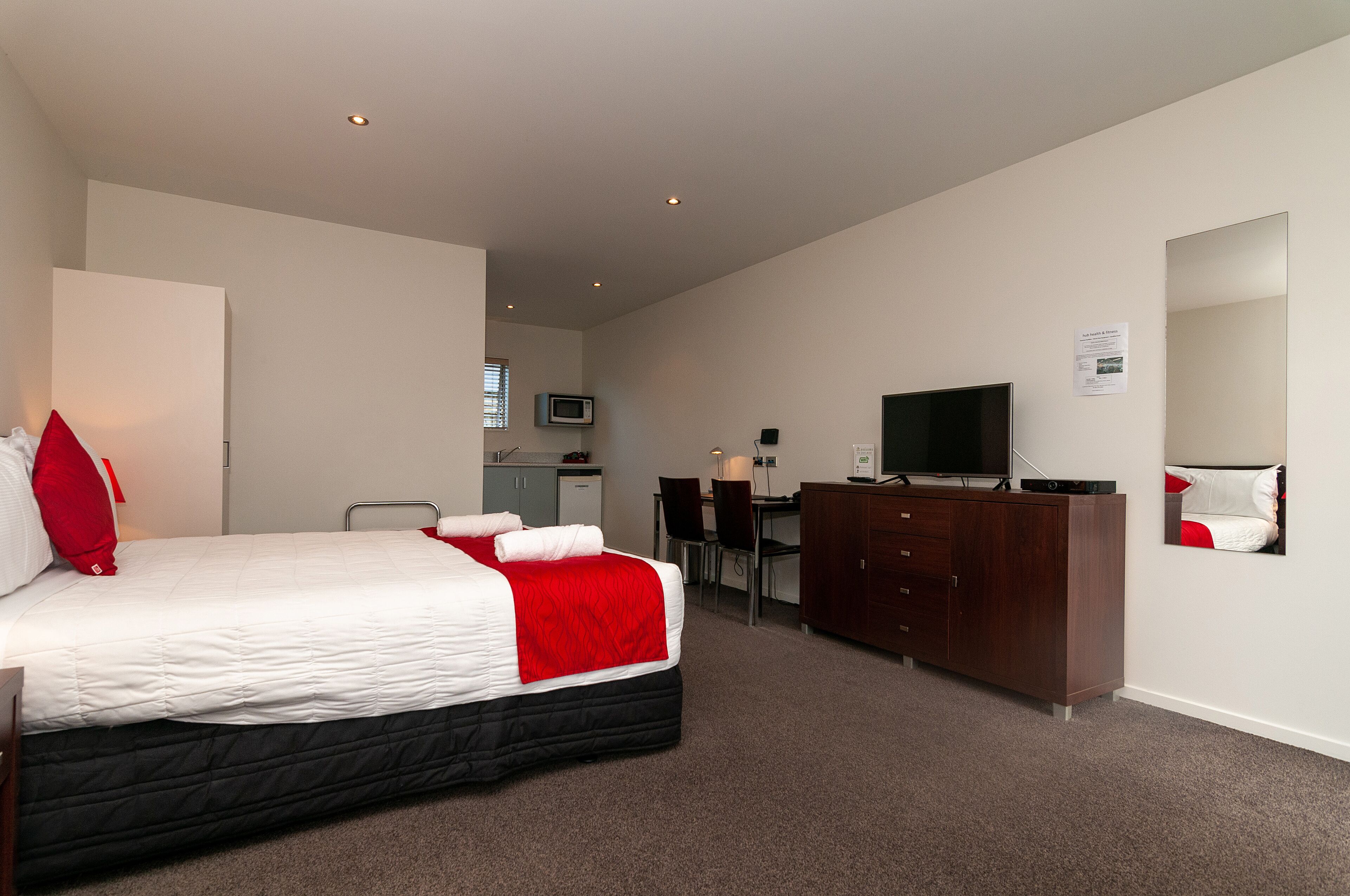 Quarto de hotel com cama, escrivaninha, televisão e espelho.