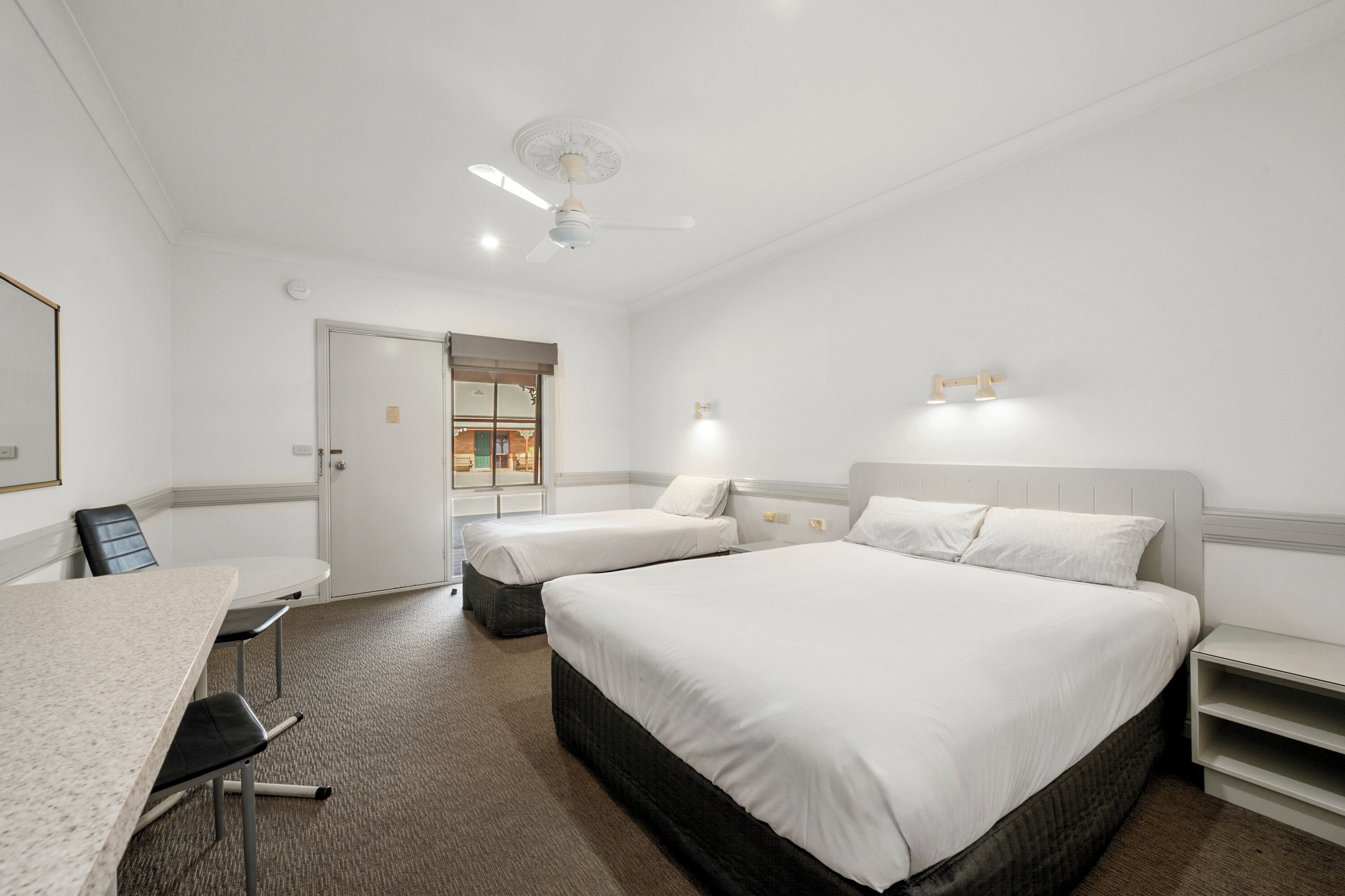 Quarto de hotel com duas camas, uma mesa e uma cadeira.