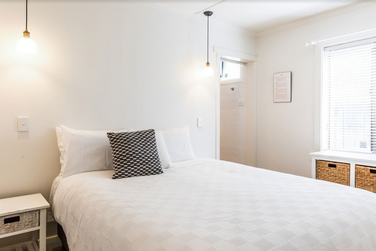 Um quarto com uma cama, mesas de cabeceira, uma janela com persianas e uma porta.