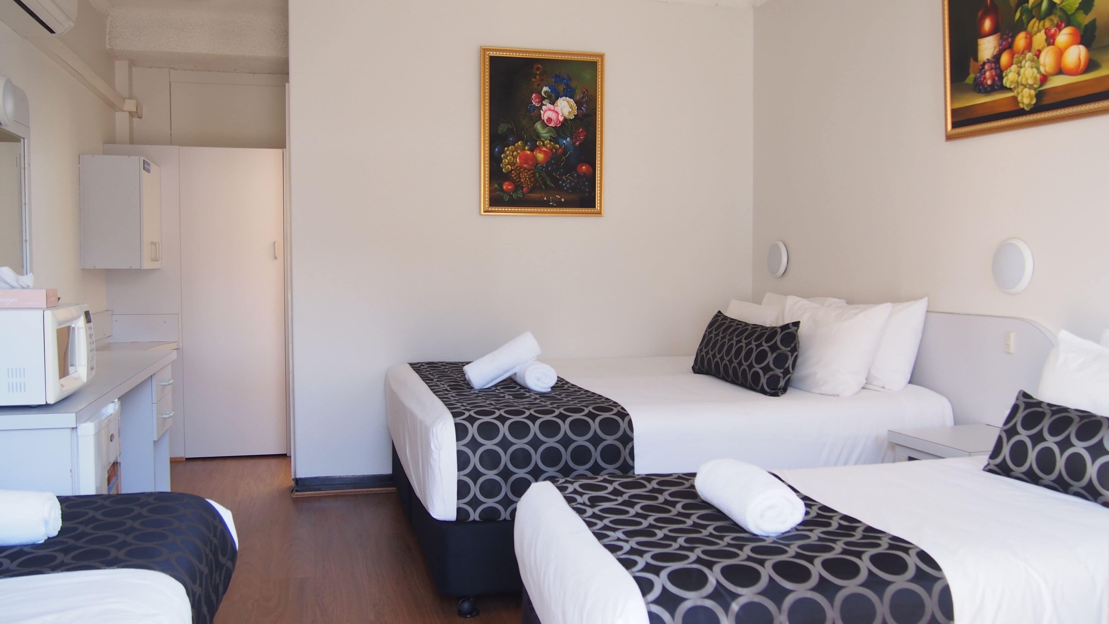 Quarto de hotel com duas camas, uma kitchenette pequena e um quadro na parede.