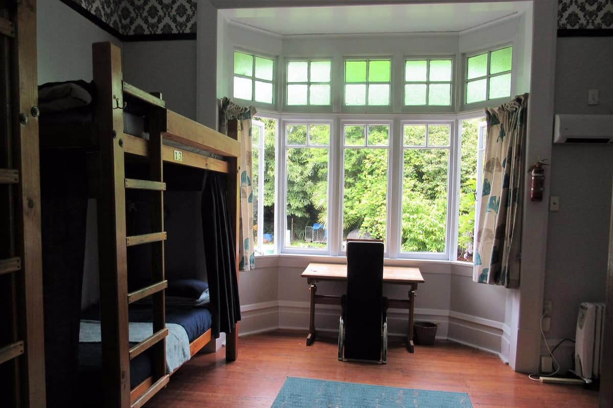 Quarto com beliche, escrivaninha e janela saliente com cortinas.