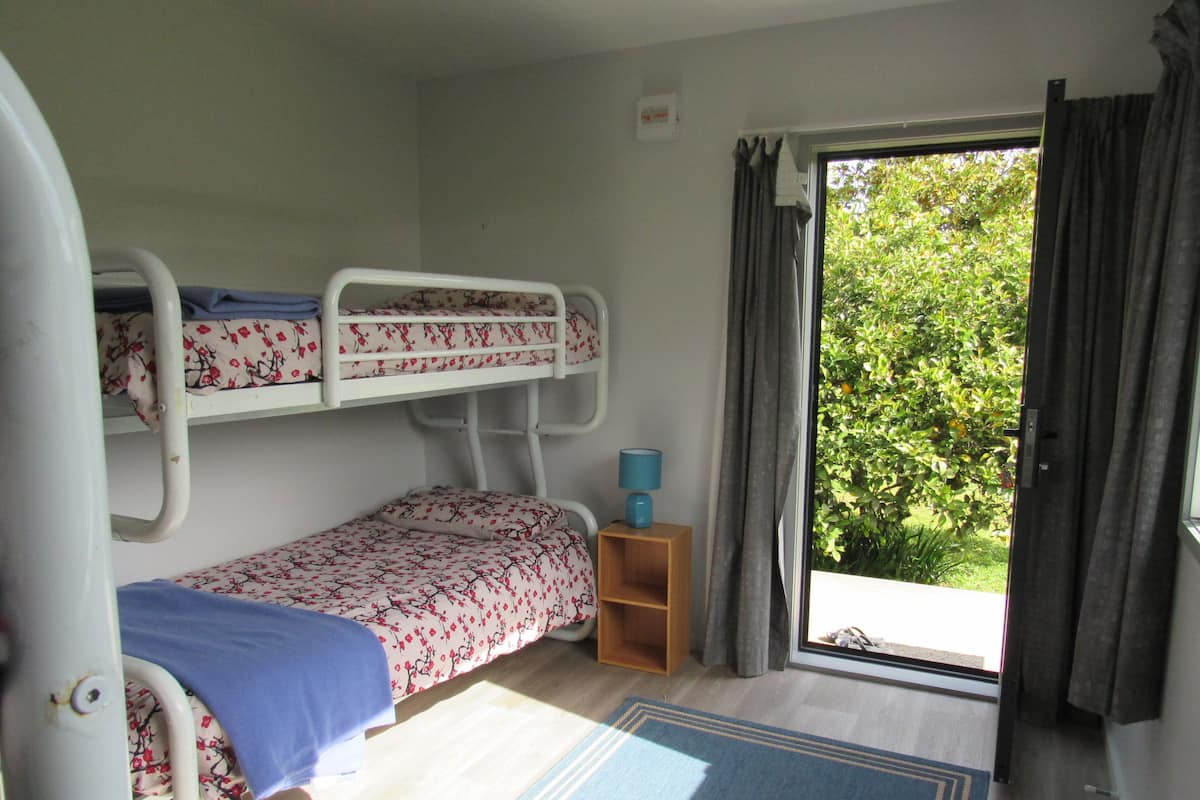 Quarto com beliches, uma mesinha com abajur e vista para o verde pela janela.