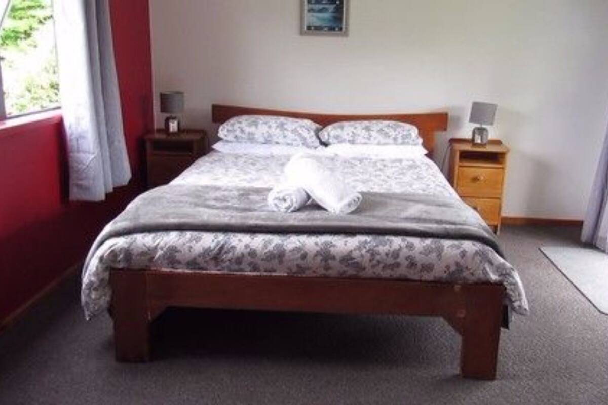Uma cama bem arrumada com colcha estampada e almofadas, uma cabeceira de madeira e duas mesas de cabeceira com abajures.