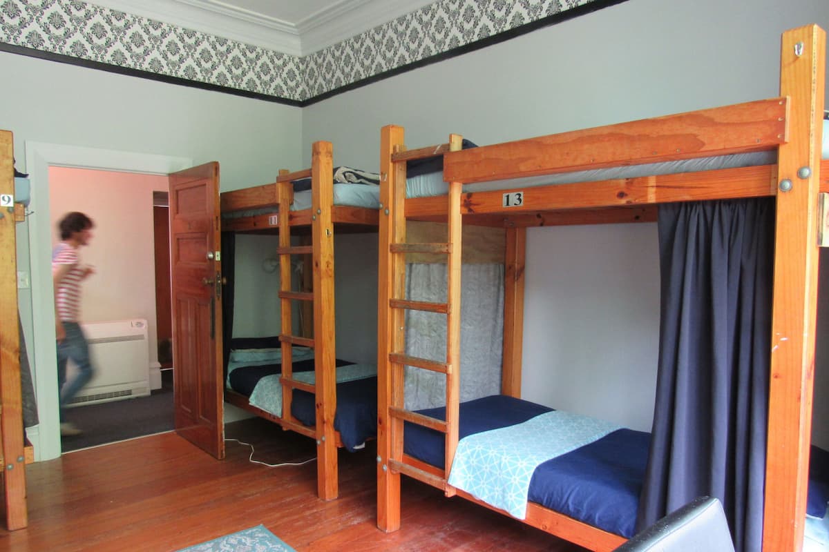 Um quarto de refeitório com beliches, numerados de 9 a 13, piso de madeira e papel de parede estampado.