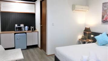 Quarto de hotel compacto com cozinha compacta, uma cama e toalhas dobradas, e um abajur.